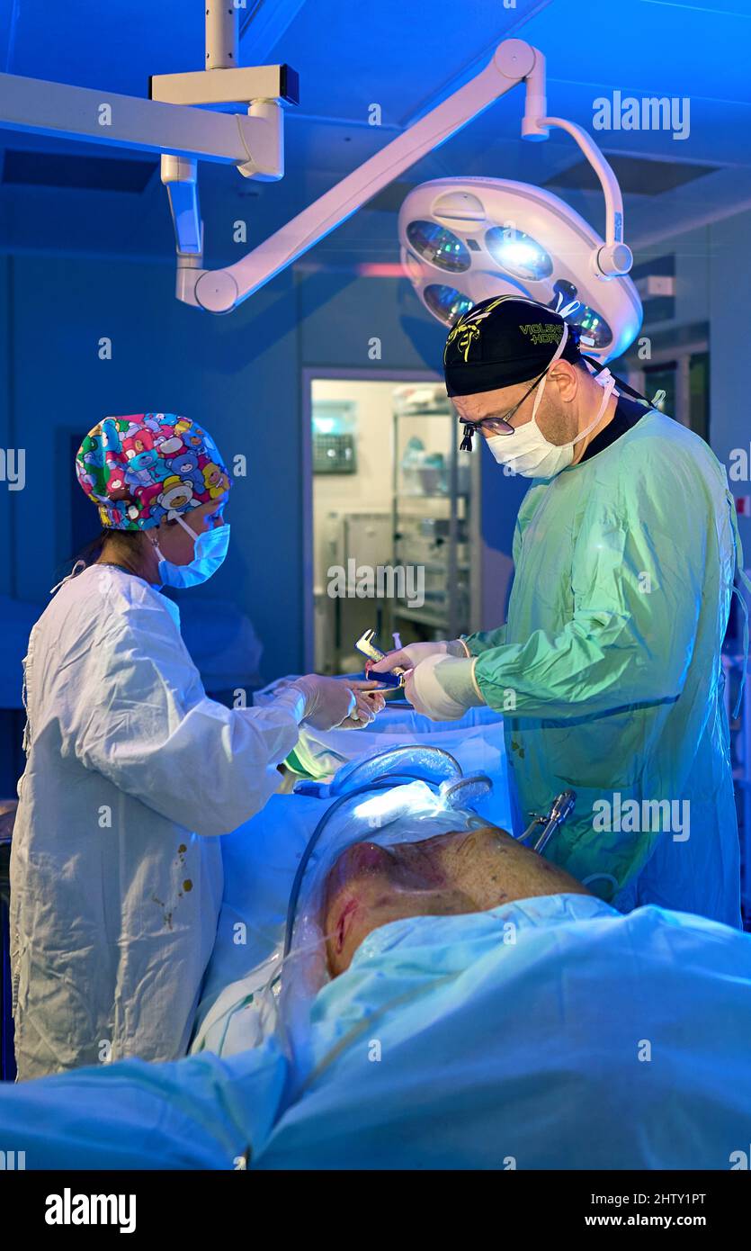 surgeon and an assistant operate on a patient in a blue operating room ...