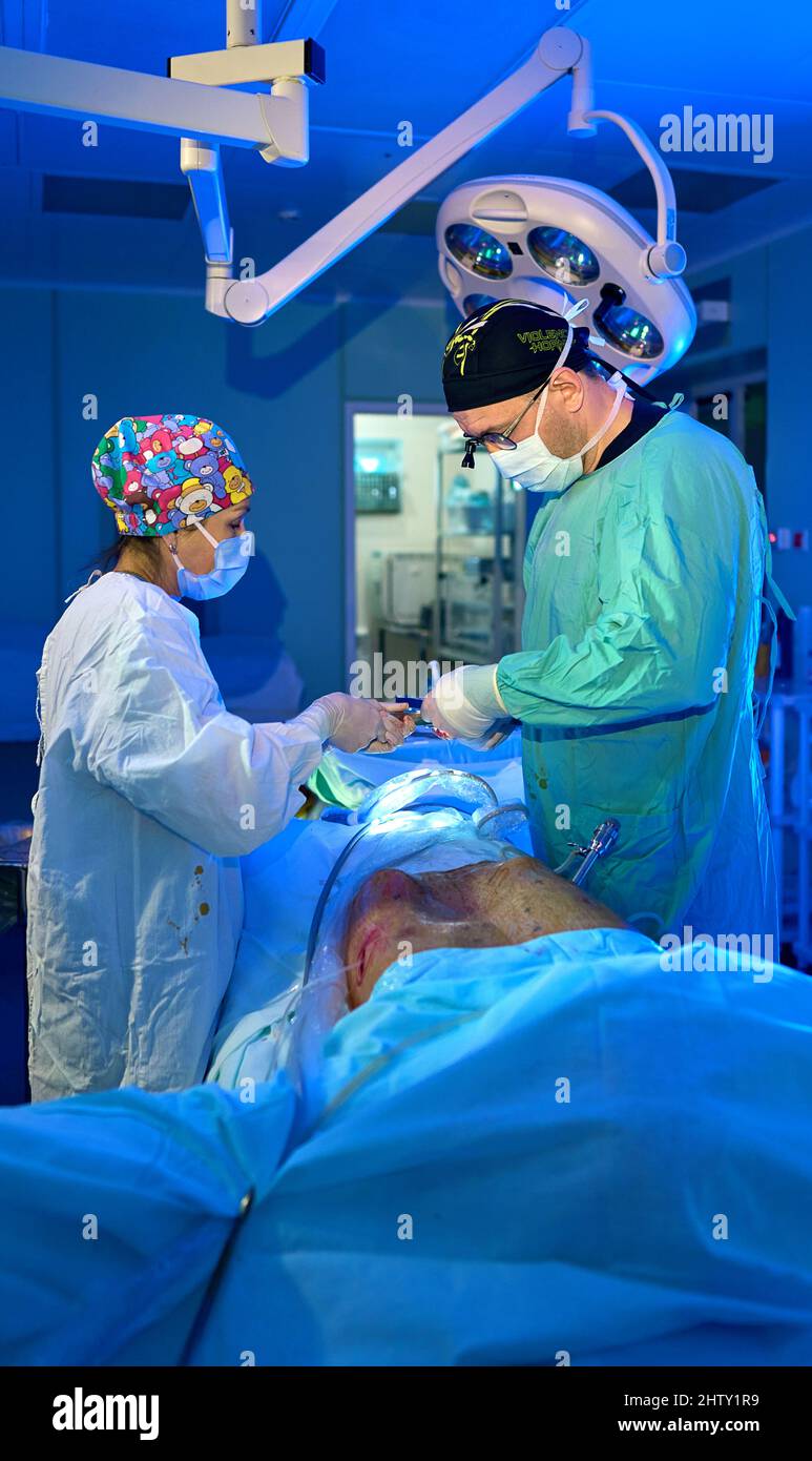 surgeon and an assistant operate on a patient in a blue operating room ...