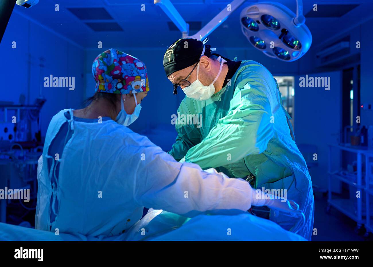 surgeon and an assistant operate on a patient in a blue operating room ...