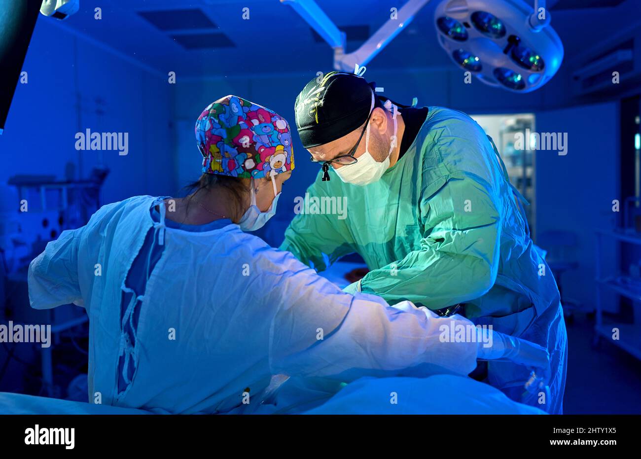 surgeon and an assistant operate on a patient in a blue operating room ...