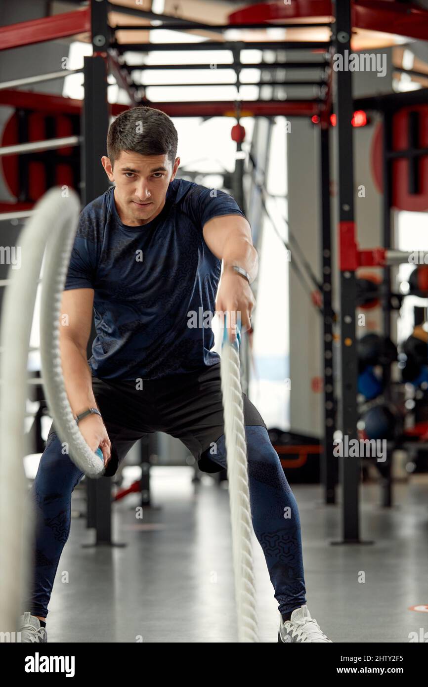 Man sitting on his toes holding a pair of battle ropes for workout. guy ...