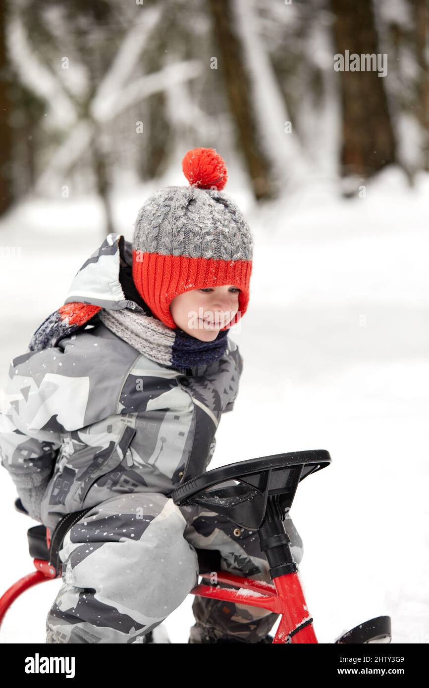 happy boy downhill on a sled in winter. a child in bright clothes sits ...