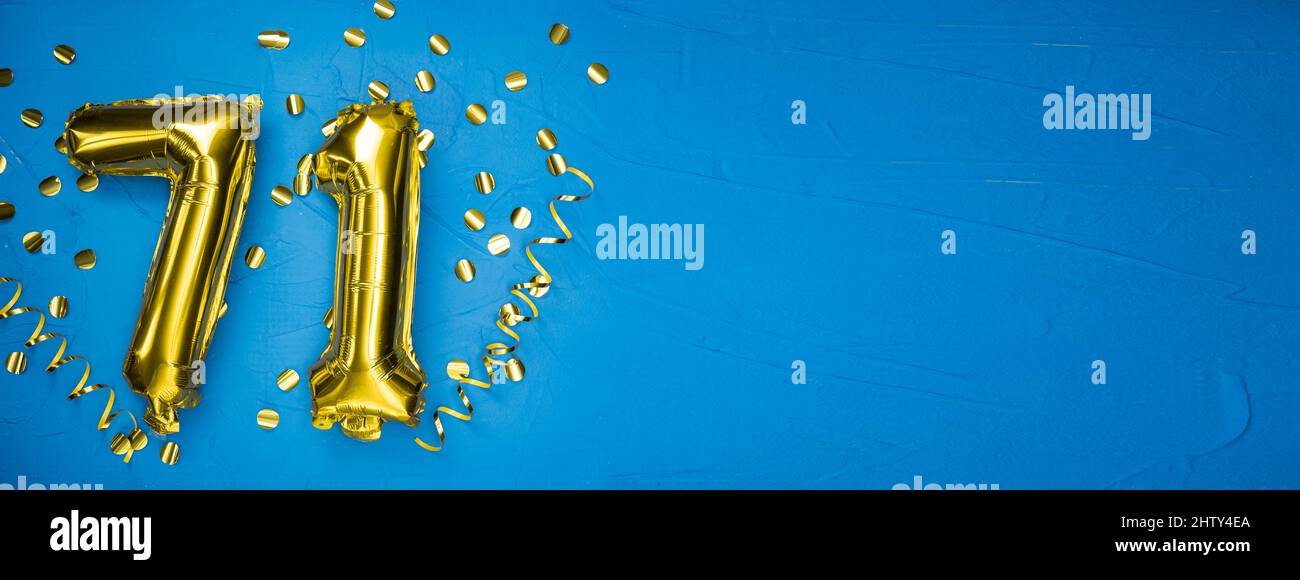 golden yellow foil balloon on blue concrete background number seventy one. Birthday or ...
