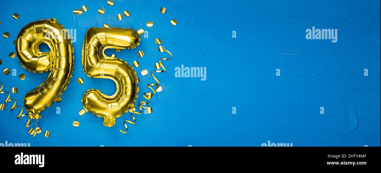 golden yellow foil balloon on blue concrete background number ninety five. Birthday or ...
