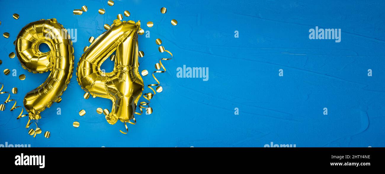 golden yellow foil balloon on blue concrete background number ninety four. Birthday or ...