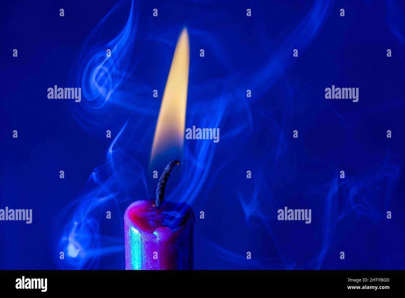 Closeup shot of the single red candle flame with the smoke on the blue ...