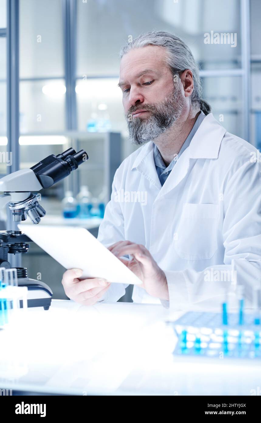 Bearded scientist using digital tablet for analyzing samples in test ...