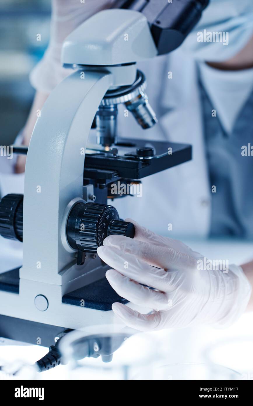Close-up of scientist adjusting the lenses of a microscope during medical exam in laboratory ...