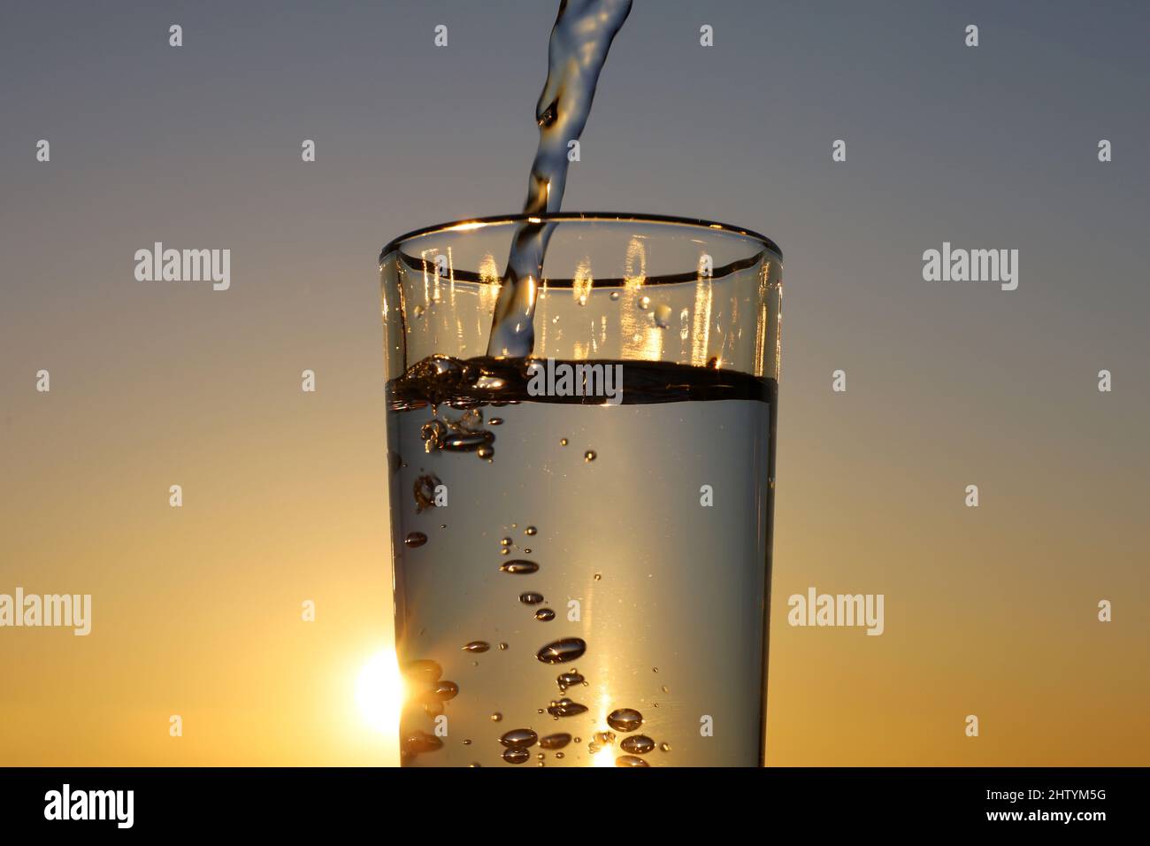 Clean water pouring into drinking glass on sunset sky background ...