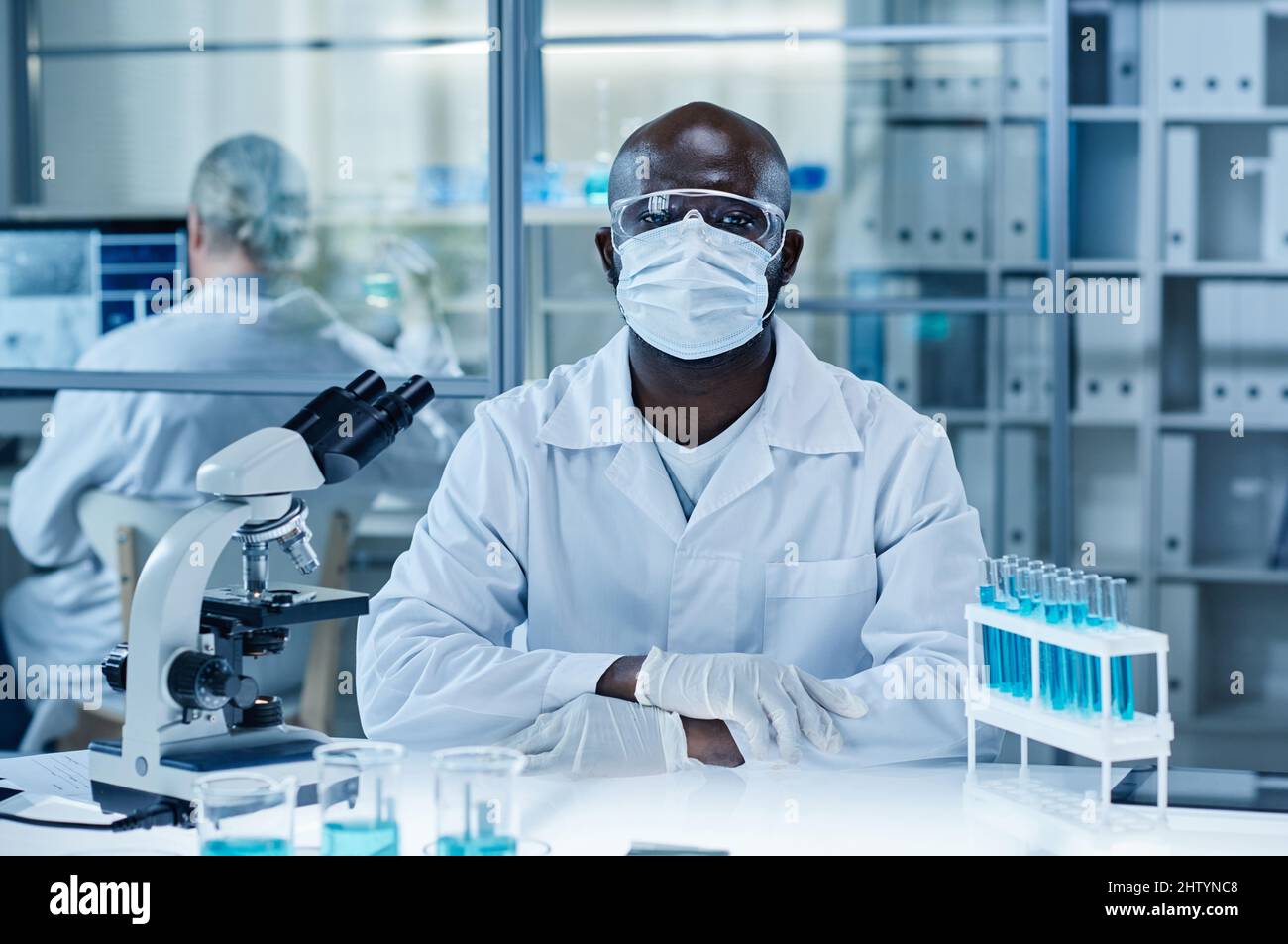 Portrait of African researcher in mask and lab coat looking at camera ...