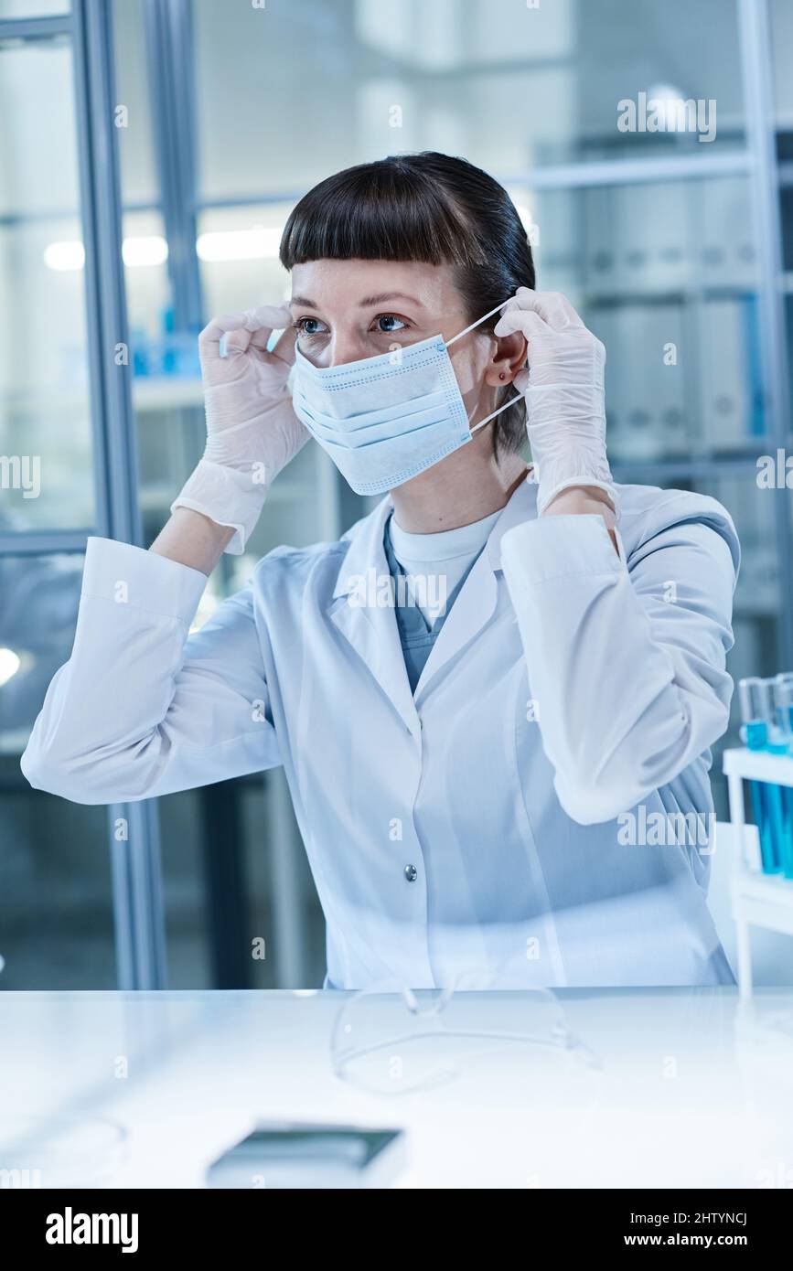 Female scientist in lab coat putting the mask on her face before work ...