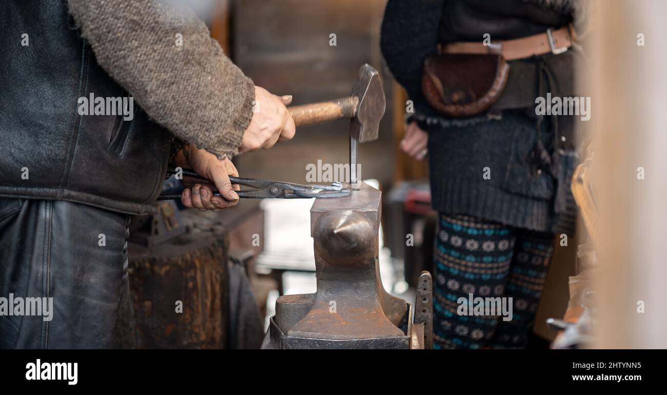 An anonymous smith, blacksmith forging a horseshoe hammering, hitting ...