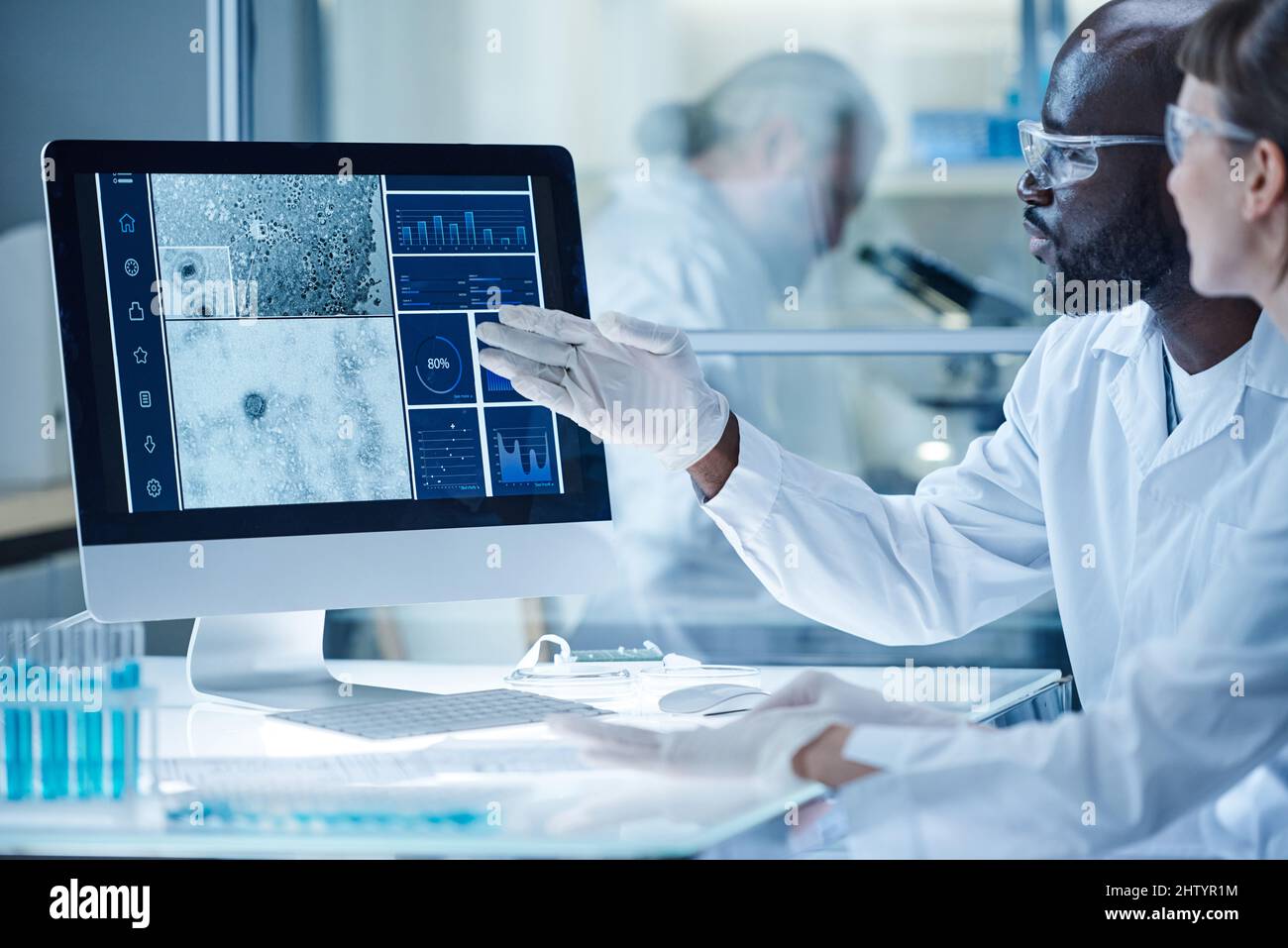 African male scientist pointing at computer monitor with micro image of ...