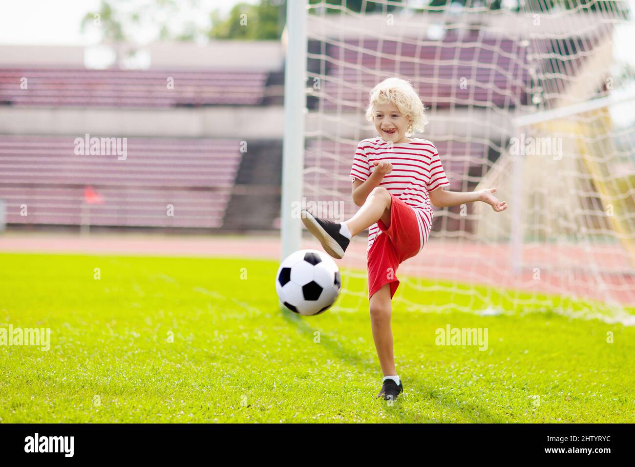 Kids play football on outdoor stadium field. Children score a goal ...