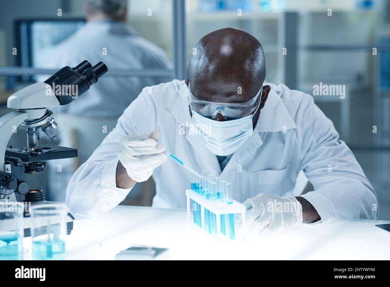 African scientist in mask taking analysis with pipette from flask ...