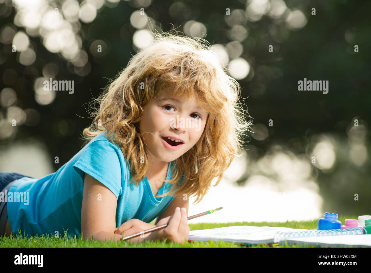 Kid draws in park laying in grass having fun on nature background ...