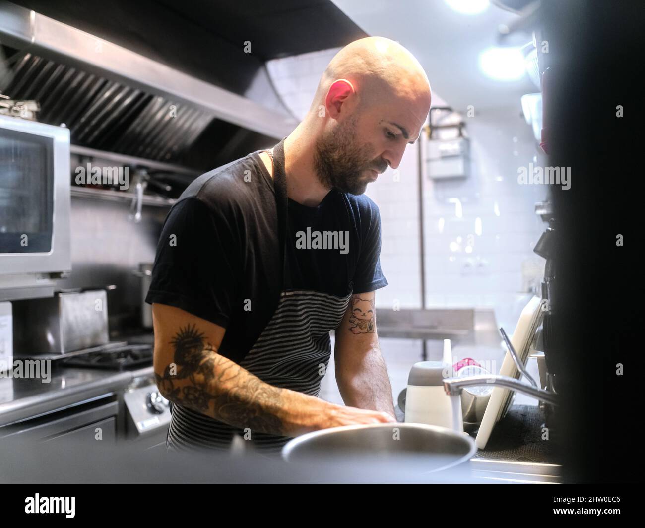 Cook with tattoos and apron working inside a kitchen Stock Photo - Alamy