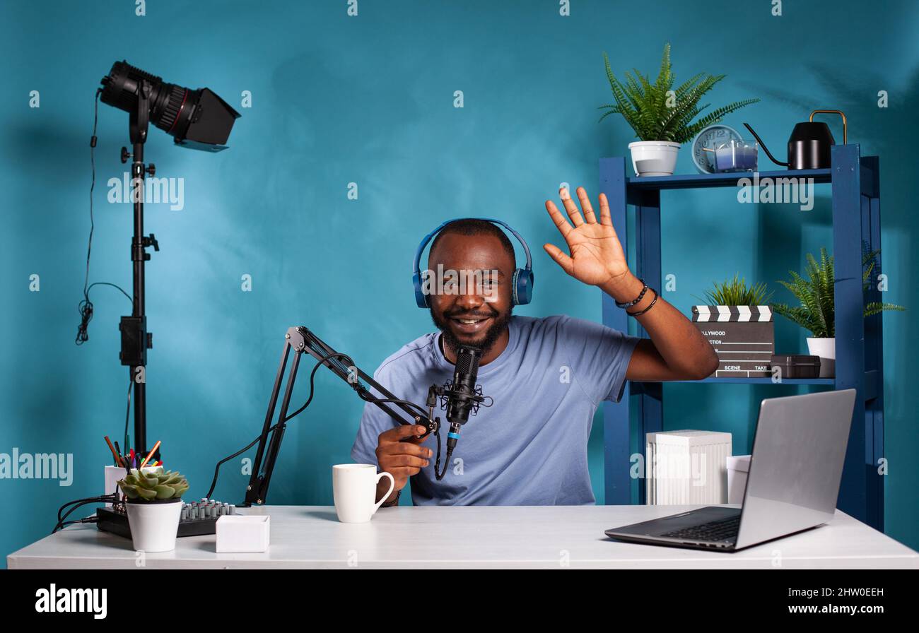 Smiling influencer wearing wireless headphones waving hello in ...