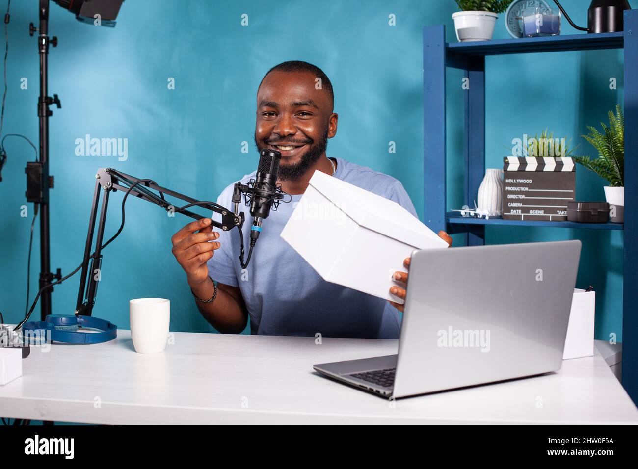 Smiling vlogger holding white box in vlogging studio with professional ...