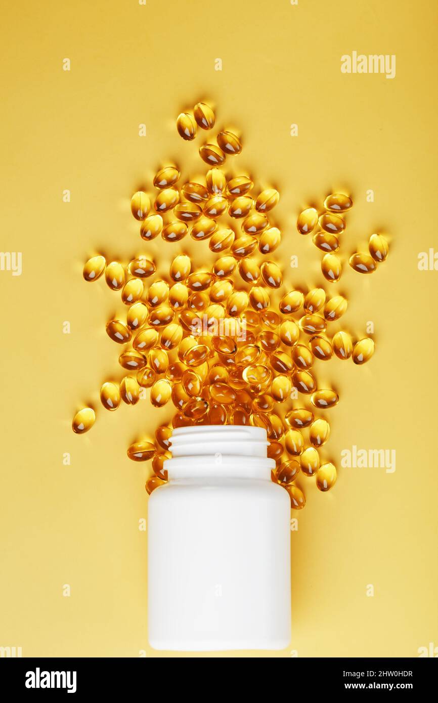 Gold Vitamin D3 capsules poured out of a jar on a yellow background ...