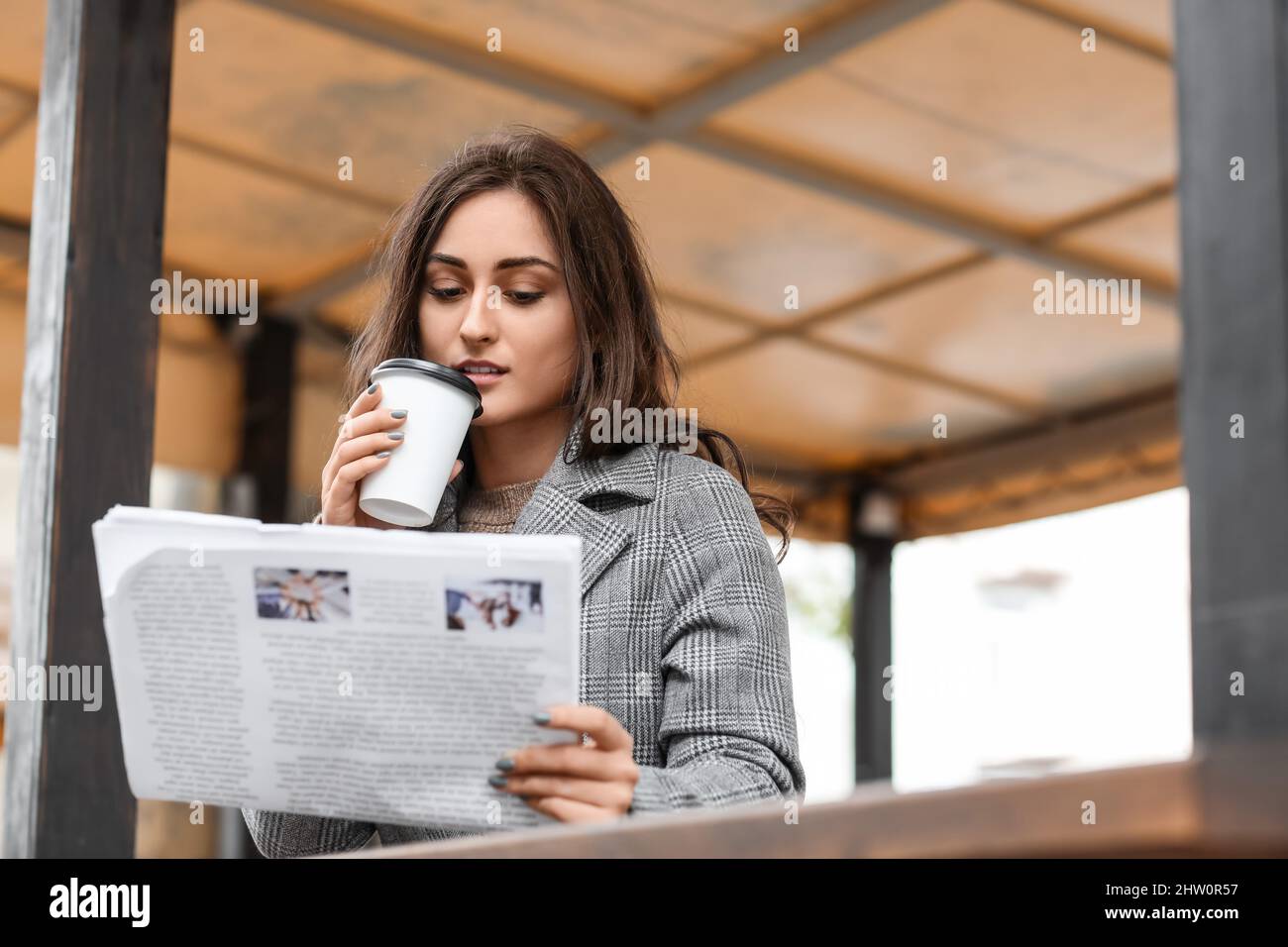 Beautiful young woman reading newspaper and drinking coffee in street ...