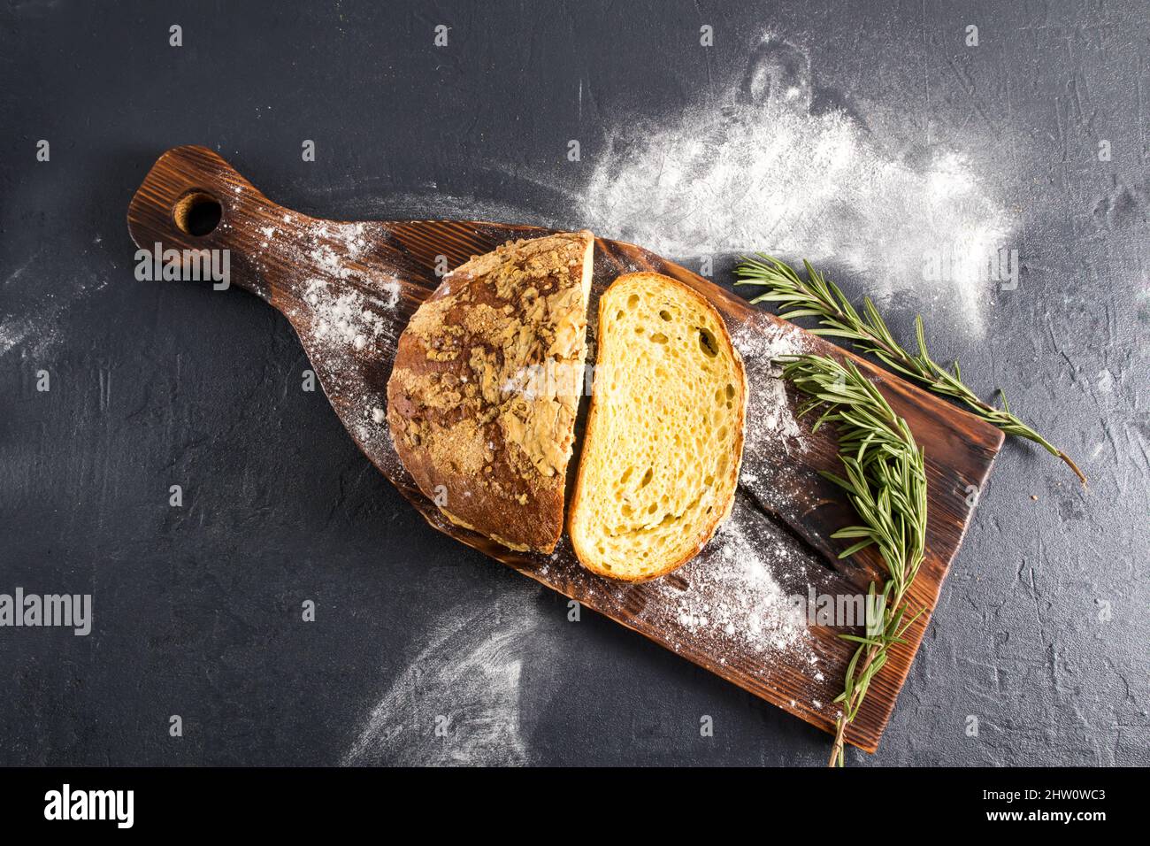 a sliced round loaf of mustard bread with rosemary on a wooden board ...