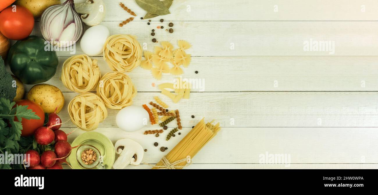 Raw pasta of various types and spices on a wooden table. View from ...