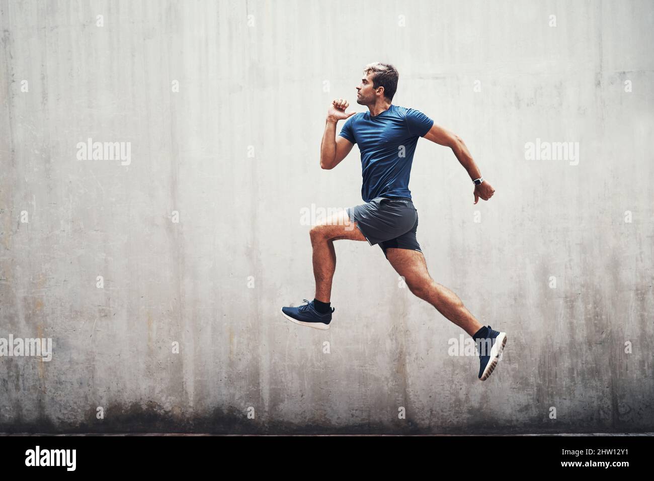 Keep up the energy. Shot of a sporty young man running against a grey ...