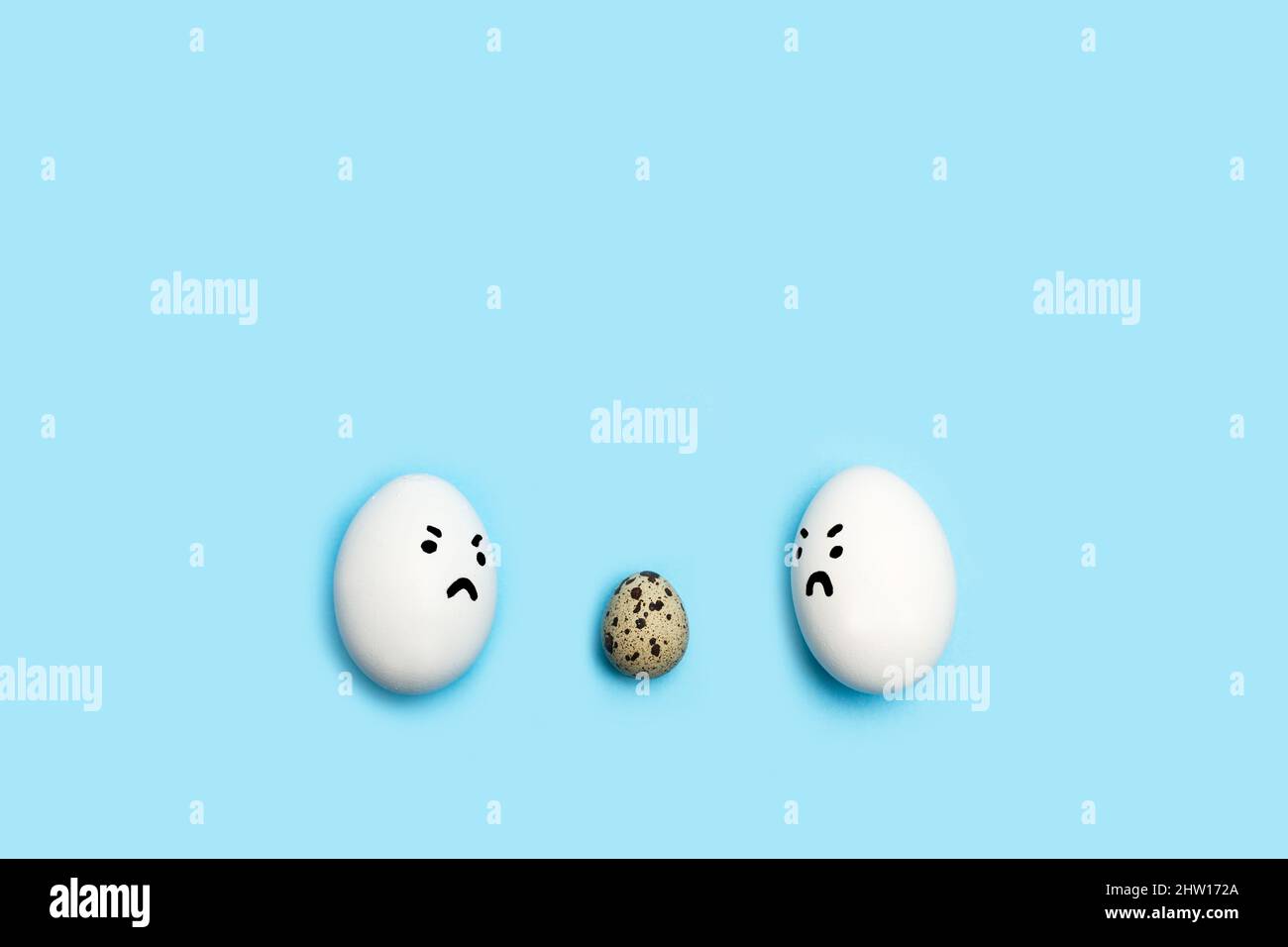 Two eggs with angry face looking at a quail egg on a blue background ...