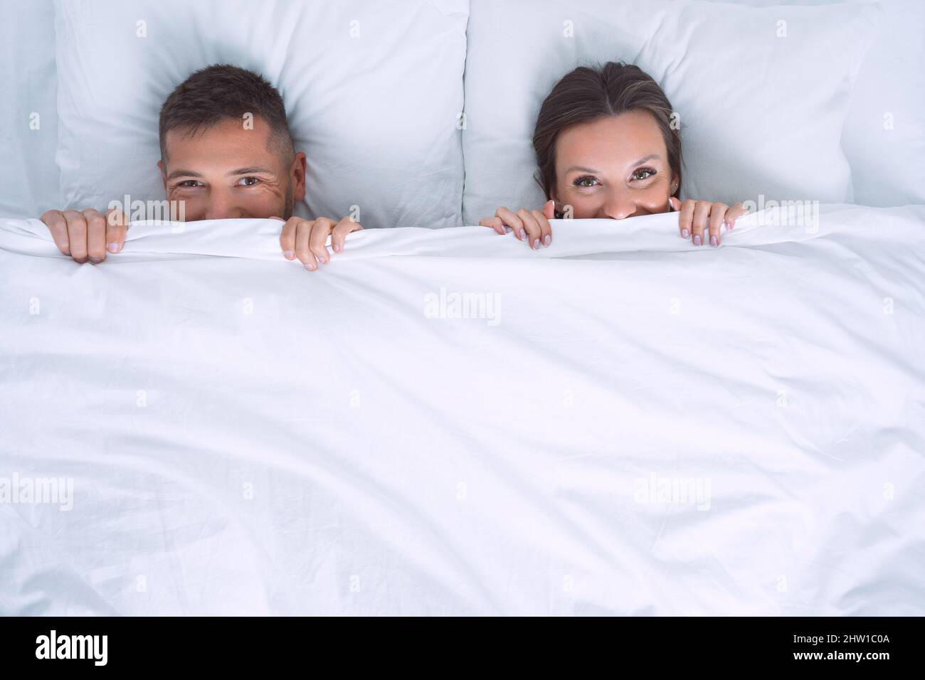 Beautiful happy couple in bed hiding and covering face with white ...
