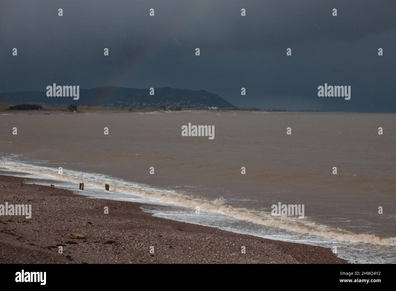 Beach and sea at Minehead with North Hill and storm clouds and rainbow ...