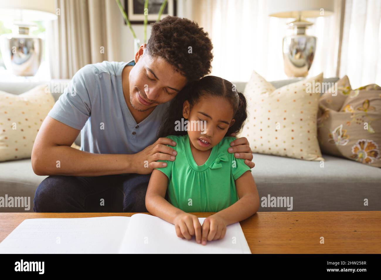Biracial blind girl touching braille while reading book by father in ...
