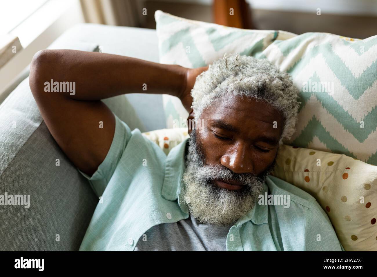 Tired african american senior man sleeping on sofa in living room at ... Tired african american senior man sleeping on sofa in living room at ...