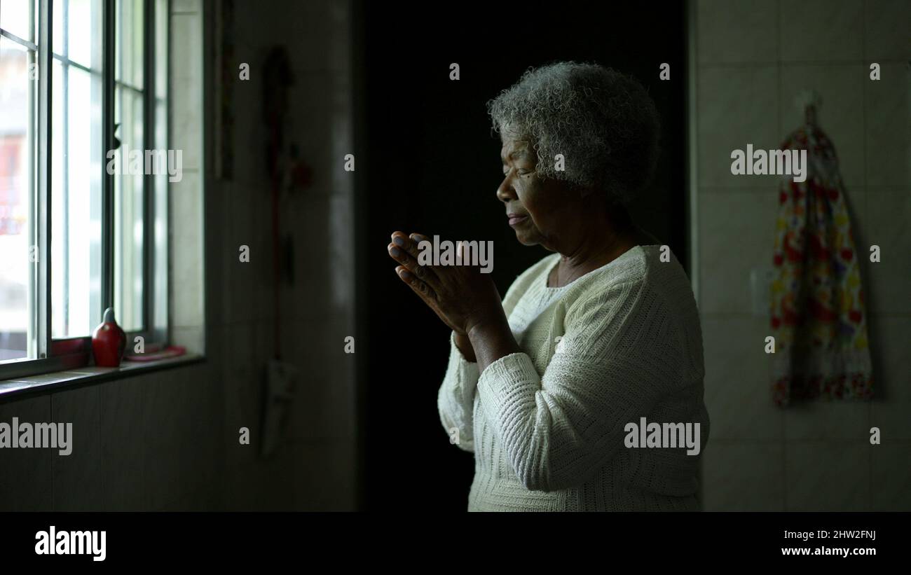 A contemplative senior black woman praying to God at home Stock Photo ...