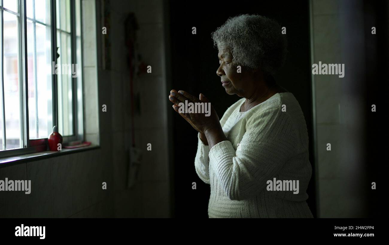 A contemplative senior black woman praying to God at home Stock Photo ...