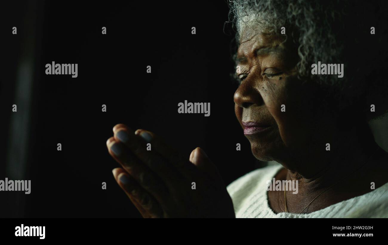 A spiritual older woman praying to God a senior African person prays ...