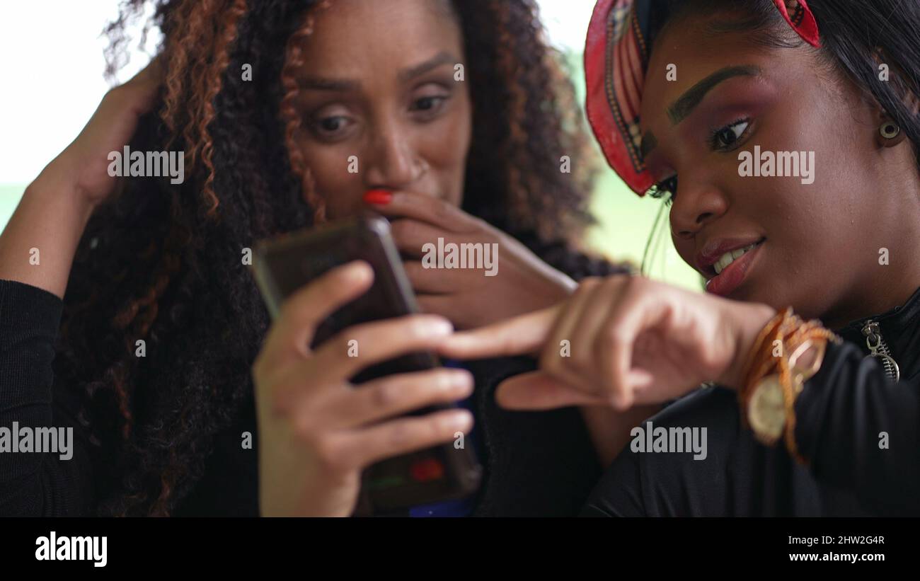 A teen daughter showing screen to mother looking at cellphone together ...