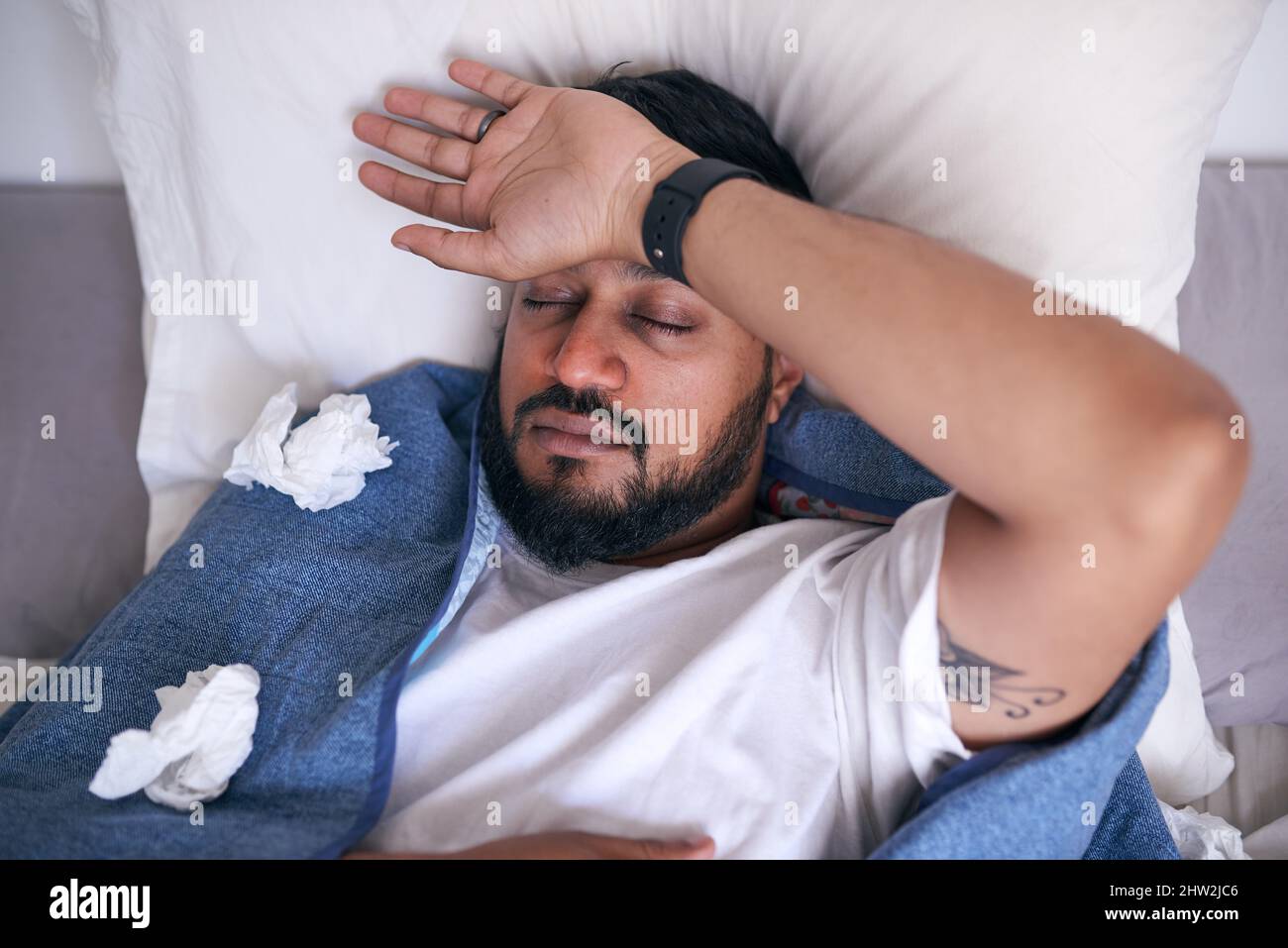 An overhead shot of a sick man in bed with his hand to his forehead ...