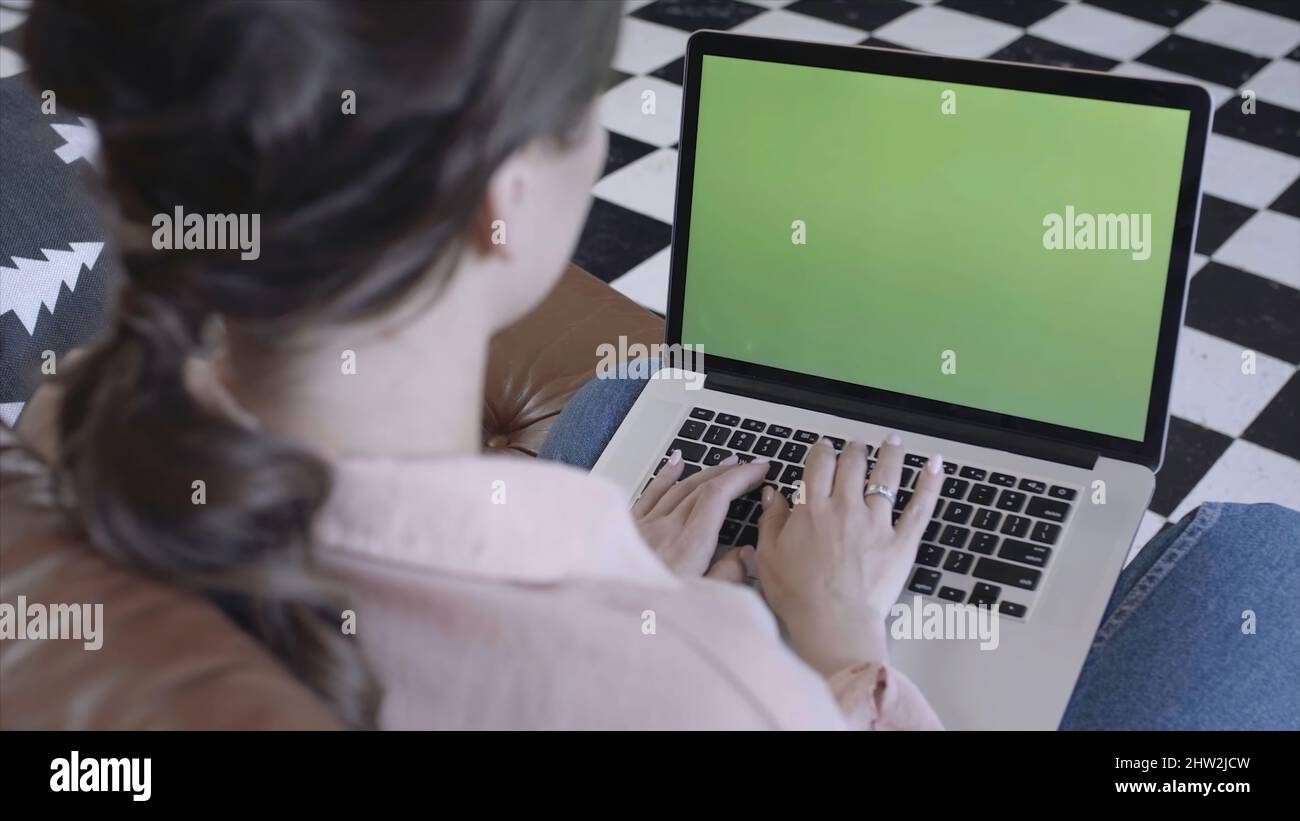 View of young woman in pink at home typing on the keyboard and looking ...