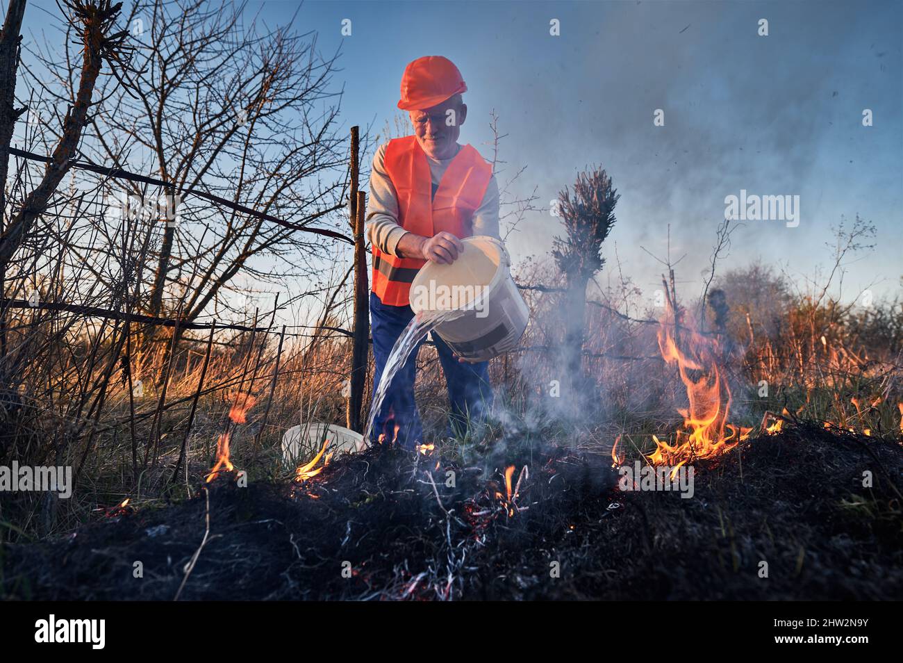 Firefighter ecologist fighting fire in field with evening sky on ...