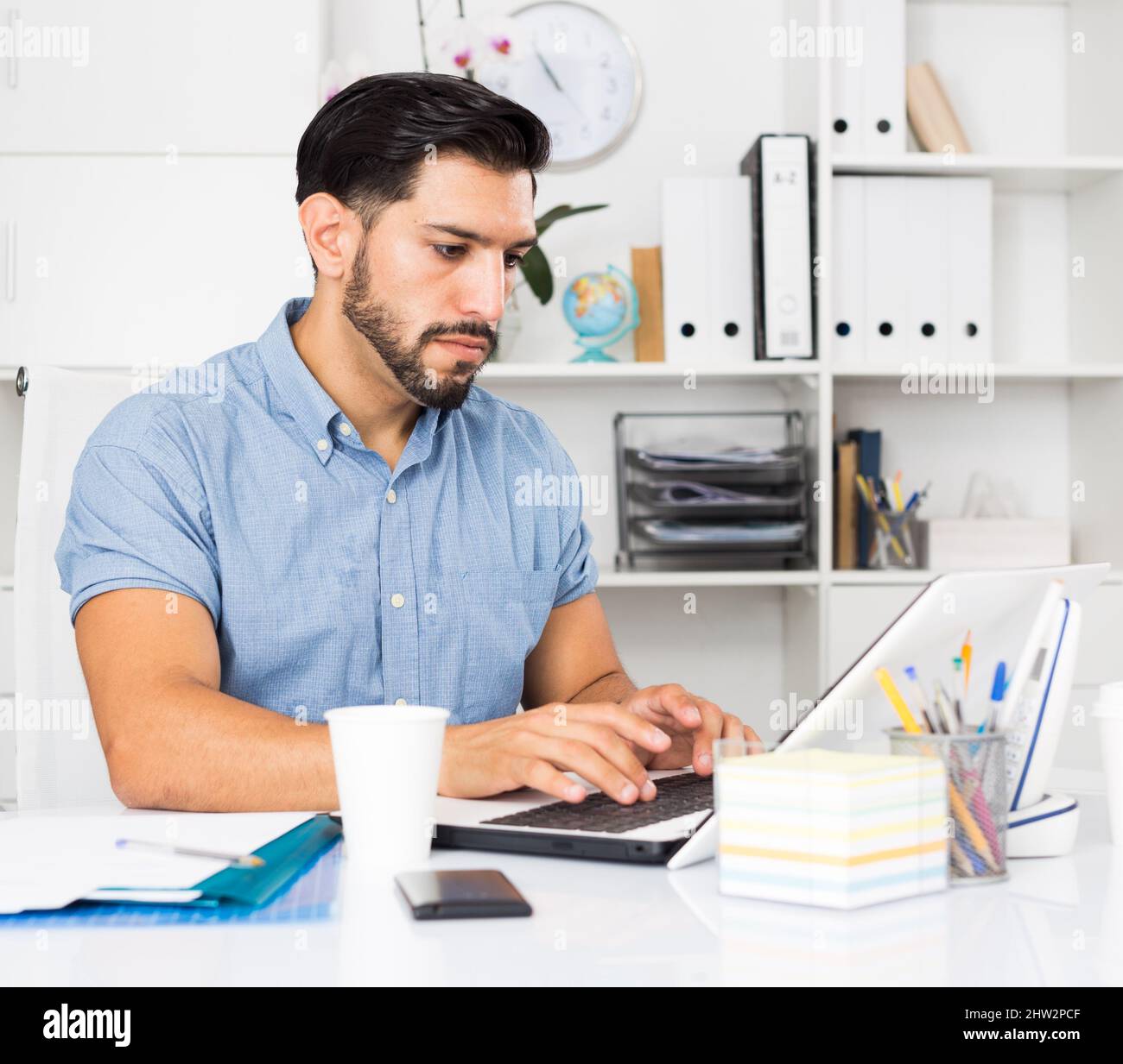 Smiling businessman is working behind laptop and reading documents ...