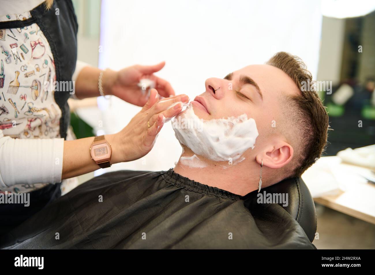 Young man shaving with straight edge razor by hairdresser in barbershop ...