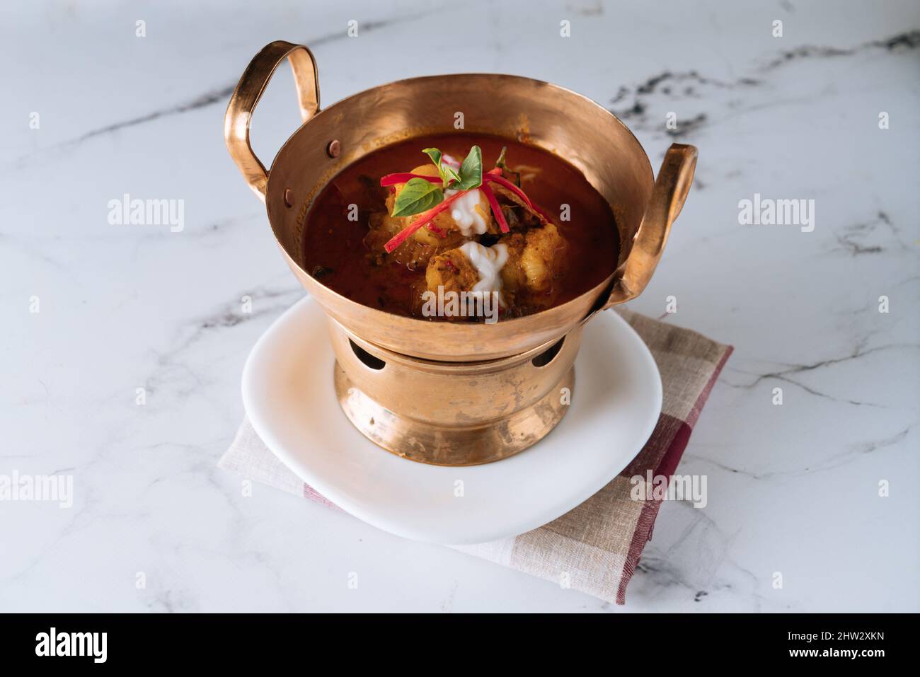 Yellow Prawn Coconut Curry in a copper stew bowl isolated on mat top ...