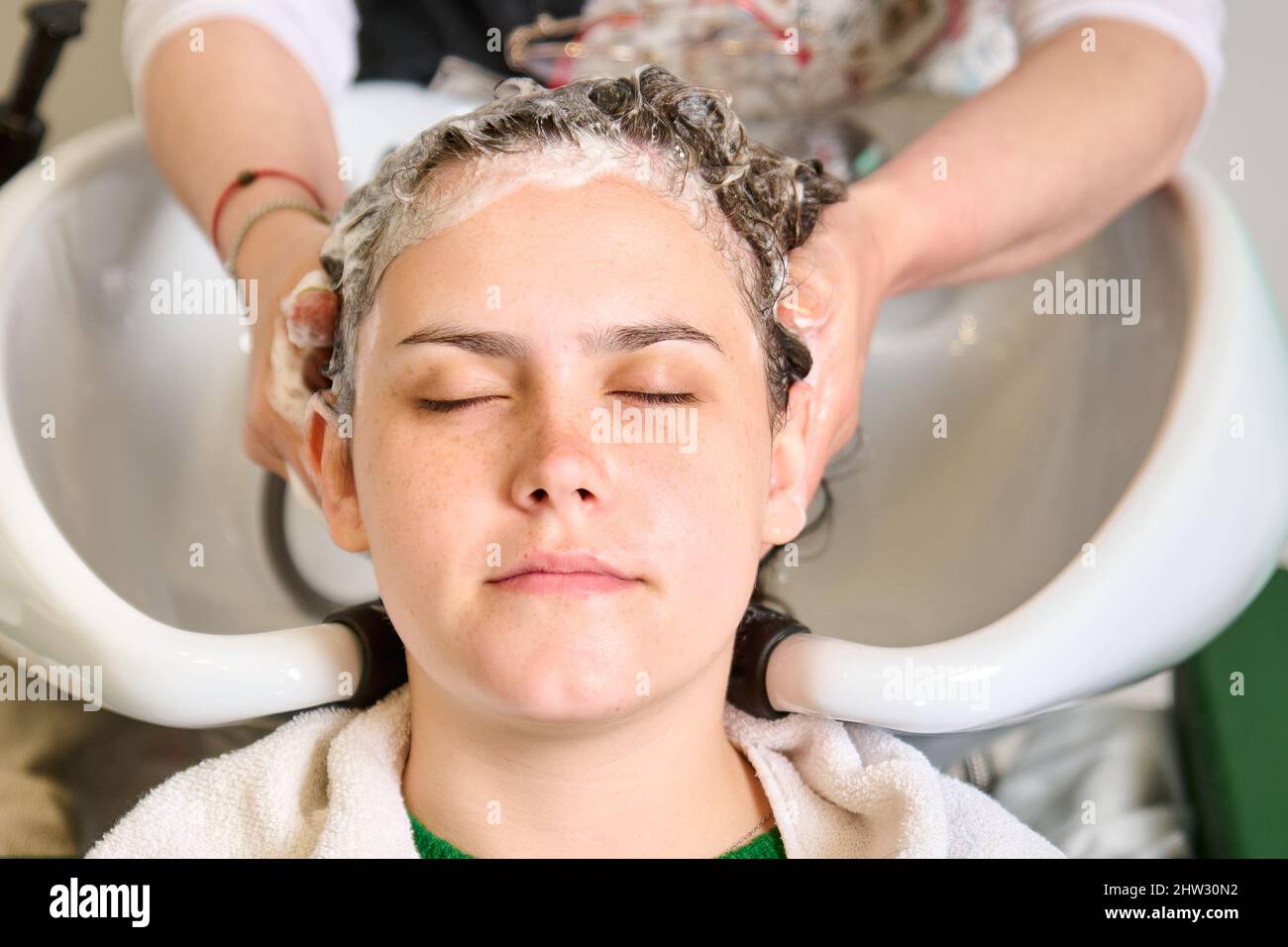 Hairdresser washes the head of a brunette girl with shampoo in the ...