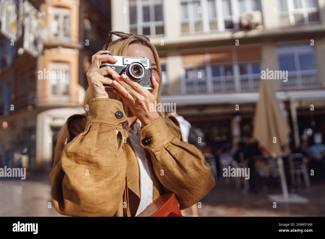 Portrait of smiling woman holding retro camera looking at viewing slot ...