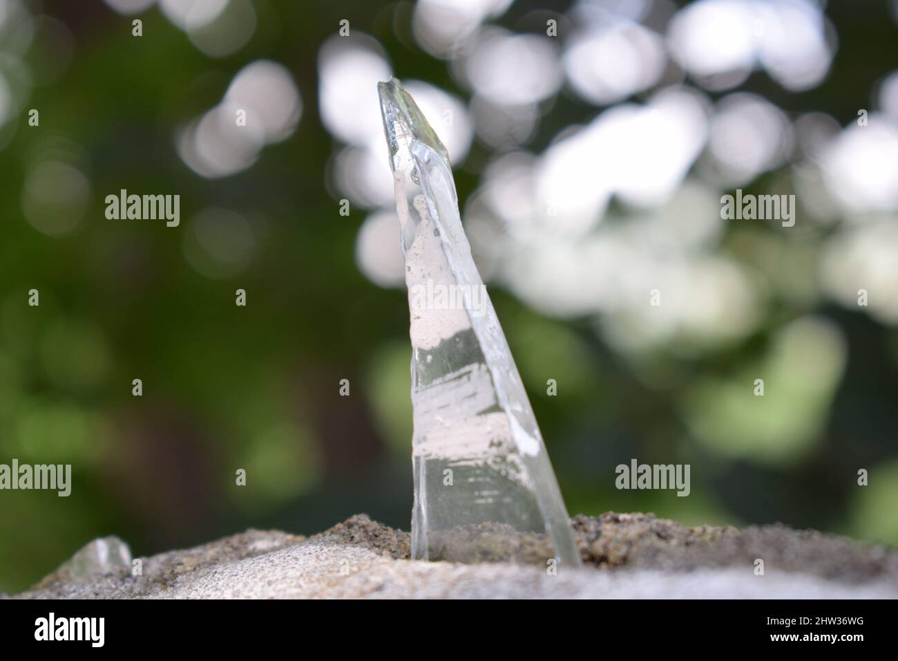 Closeup of a glass shard placed upright in sand in front of a blurred ...