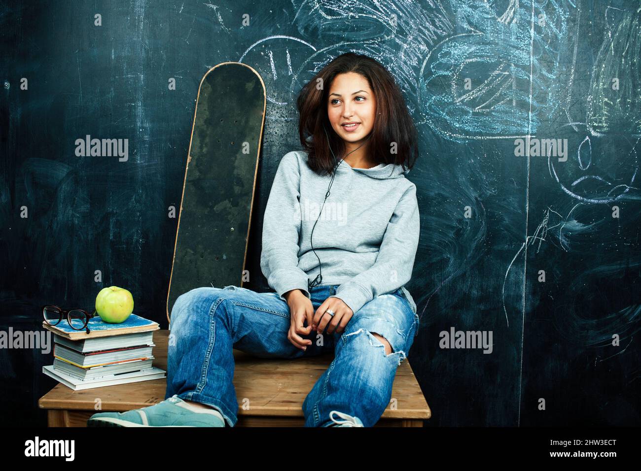 young cute teenage girl in classroom at blackboard seating on table ...