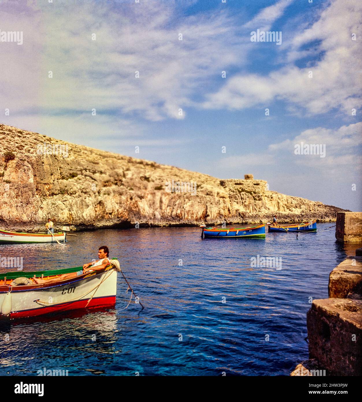 Sailor relaxing in gaily painted boat on calm seas with glorious clouds ...