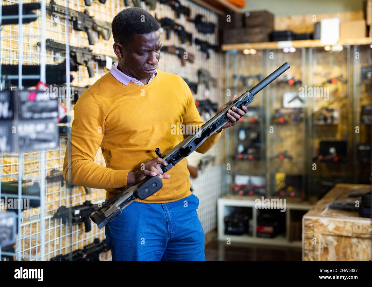 African american man chooses pump-action shotgun in gun store closeup ...