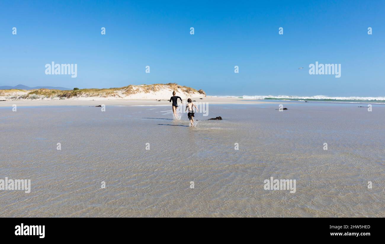 South Africa, Hermanus, Girl (16-17) and boy (8-9) running on Grotto ...